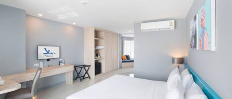 Quarto de hotel com cama, escrivaninha, cadeira e televisão na parede.