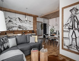 Uma sala de estar moderna com um sofá cinzento, vigas de madeira, uma área de jantar com uma mesa branca e uma grande pintura em preto e branco.
