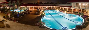 Uma grande piscina interior com várias pistas de natação, rodeada por áreas de estar ao ar livre e um alpendre coberto.