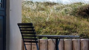 Uma cadeira e mesa de madeira em frente a um prédio, com cerca de madeira e gramado ao fundo.