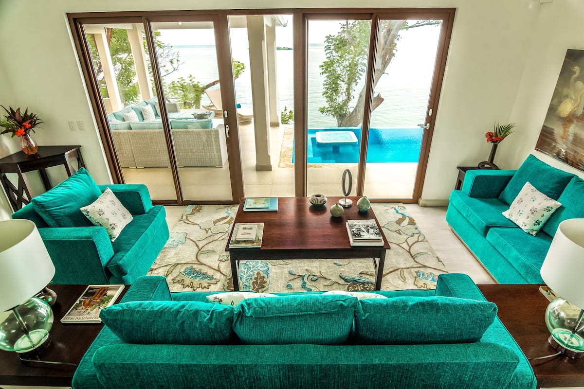 Sala de estar com sofás azul-turquesa, mesa de centro de madeira e vista para uma piscina e área de estar externa.