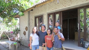 Uma família em frente a uma casa com varanda e um caminho de pedra.