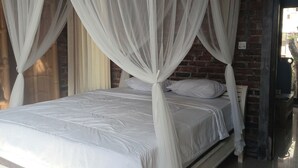 Uma cama com dossel branco e parede de tijolos ao fundo.