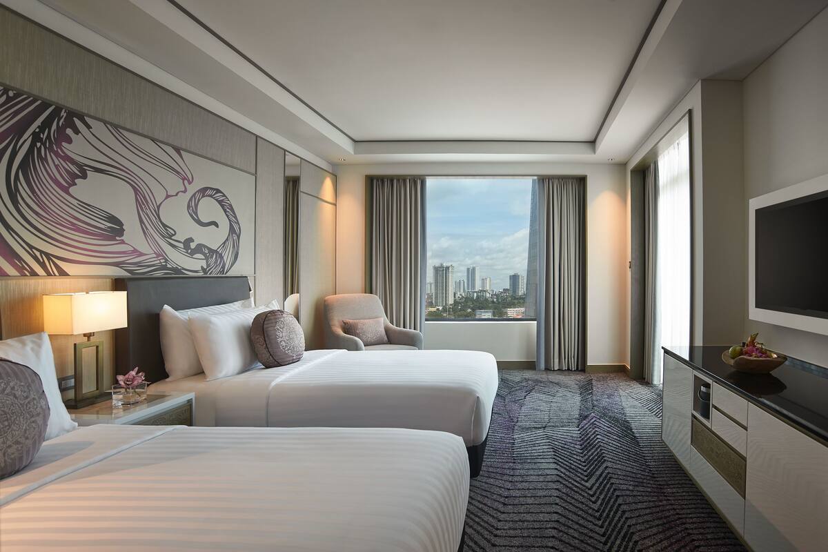 Quarto de hotel com duas camas, uma janela grande com vista para a cidade, televisão de tela plana e design moderno.