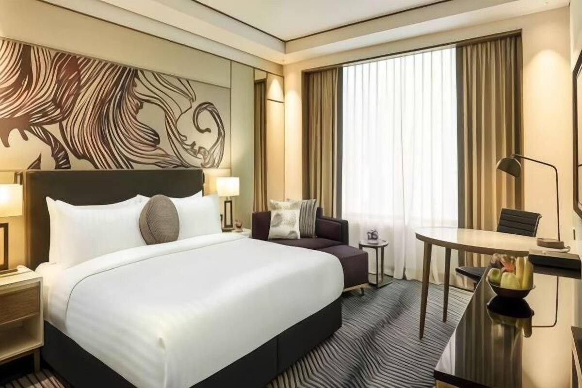 Quarto de hotel com cama grande, sofá, escrivaninha e mesa de jantar.