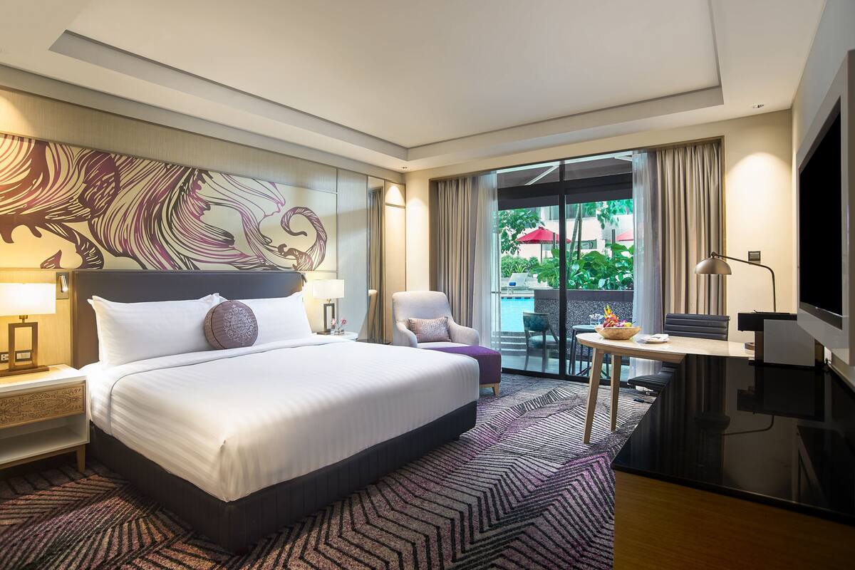 Quarto de hotel com uma cama grande, uma escrivaninha, uma cadeira e uma televisão.