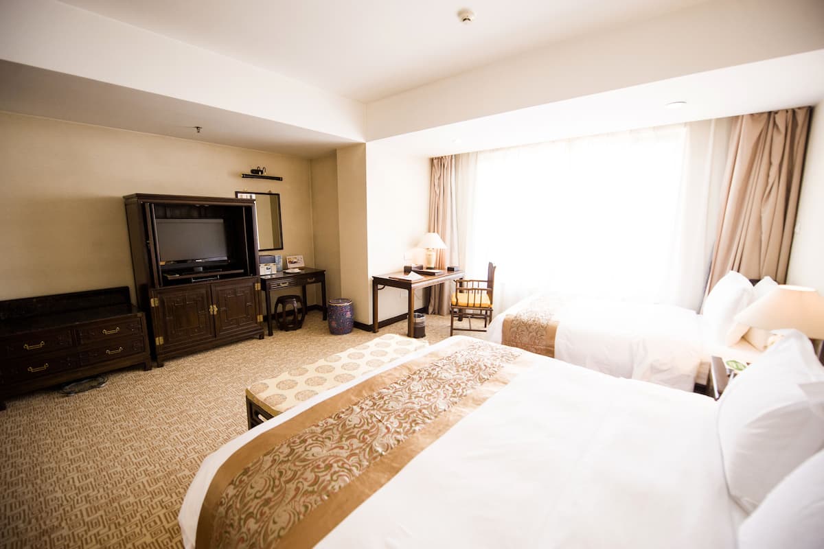 Quarto de hotel com cama, escrivaninha, televisão e janela com cortinas.