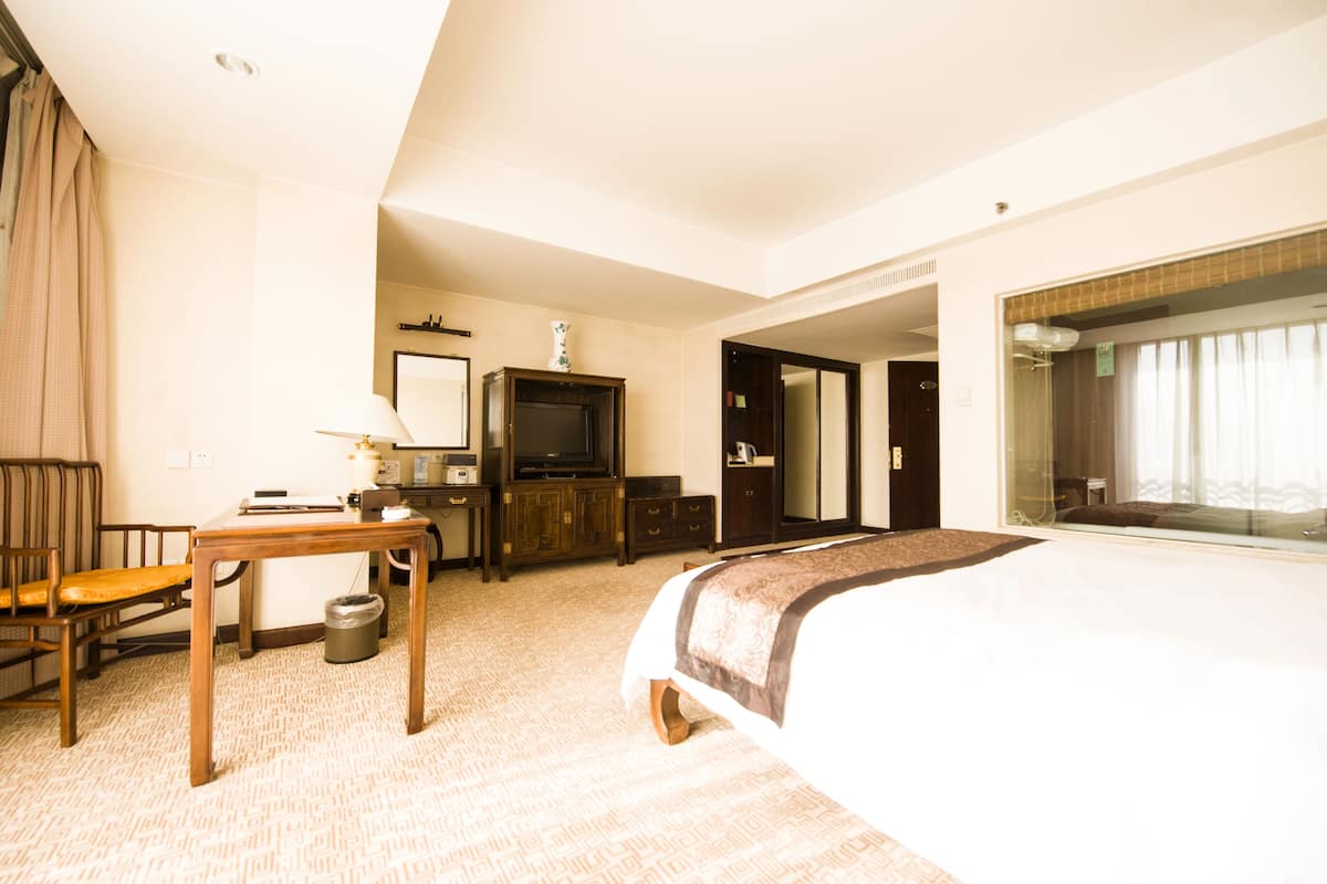 Quarto de hotel com uma cama grande, escrivaninha com luminária, televisão e guarda-roupa.