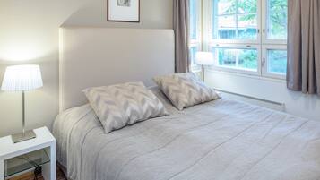 Uma cama bem arrumada com cabeceira, luminária ao lado e quadro na parede.