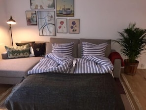 Quarto com cama, sofá, luminária, planta em vaso e obra de arte na parede.
