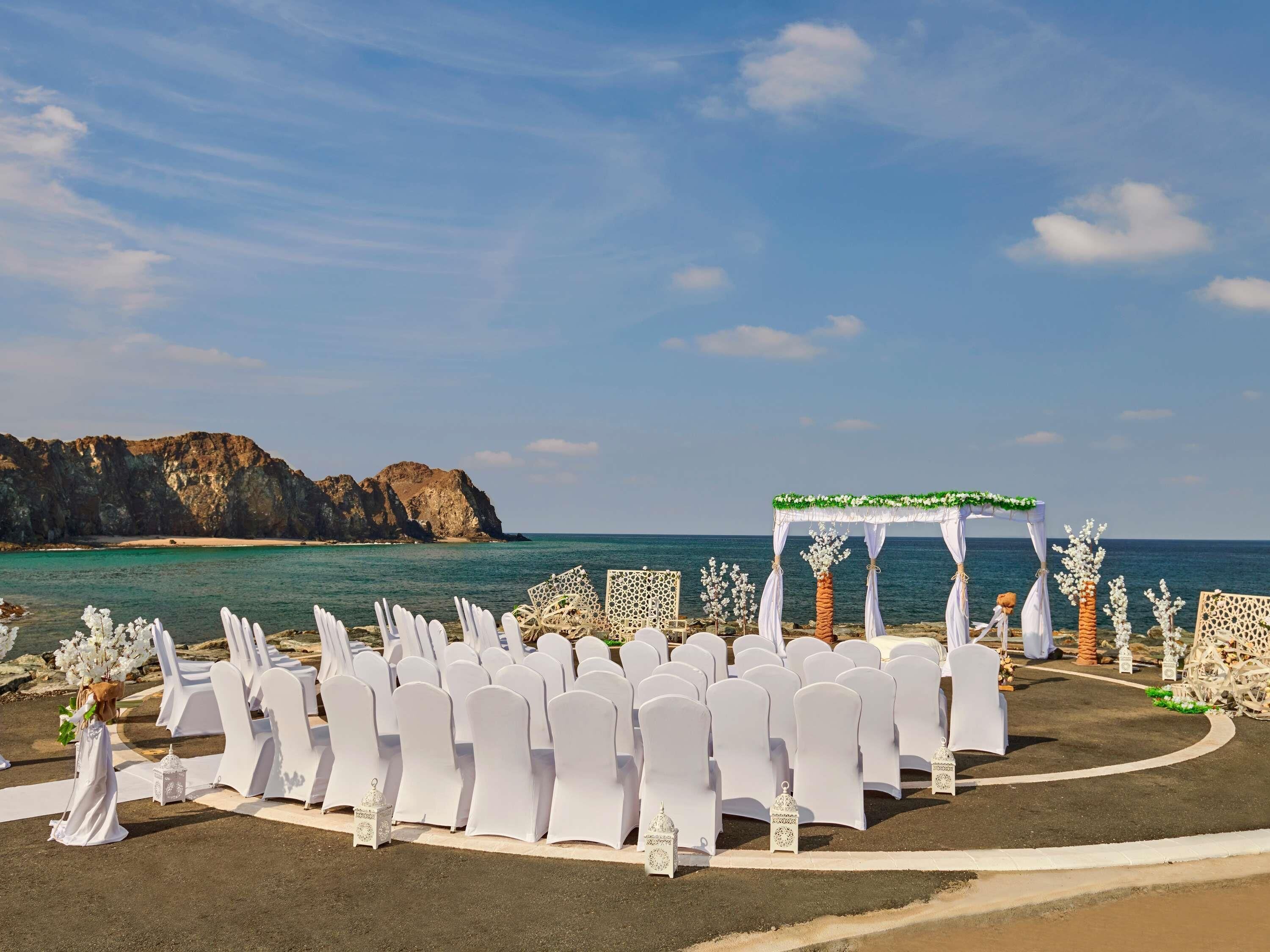 Montagem para um casamento na praia, com cadeiras brancas e um toldo, com vista para o mar.