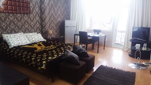 Quarto de hotel com cama, escrivaninha, cadeira, televisão e mesa de centro.