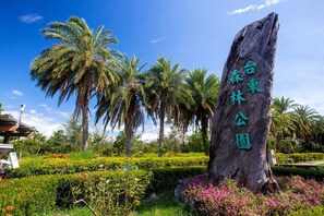 Uma grande pedra com caracteres chineses, cercada por vegetação exuberante e palmeiras.