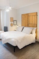 Quarto com cabeceira de madeira, colcha branca e luminária pendente.