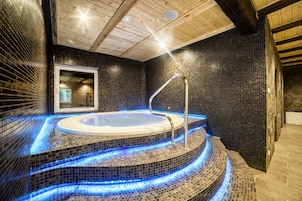 Uma banheira de hidromassagem com iluminação LED azul, teto de madeira e paredes em mosaico.