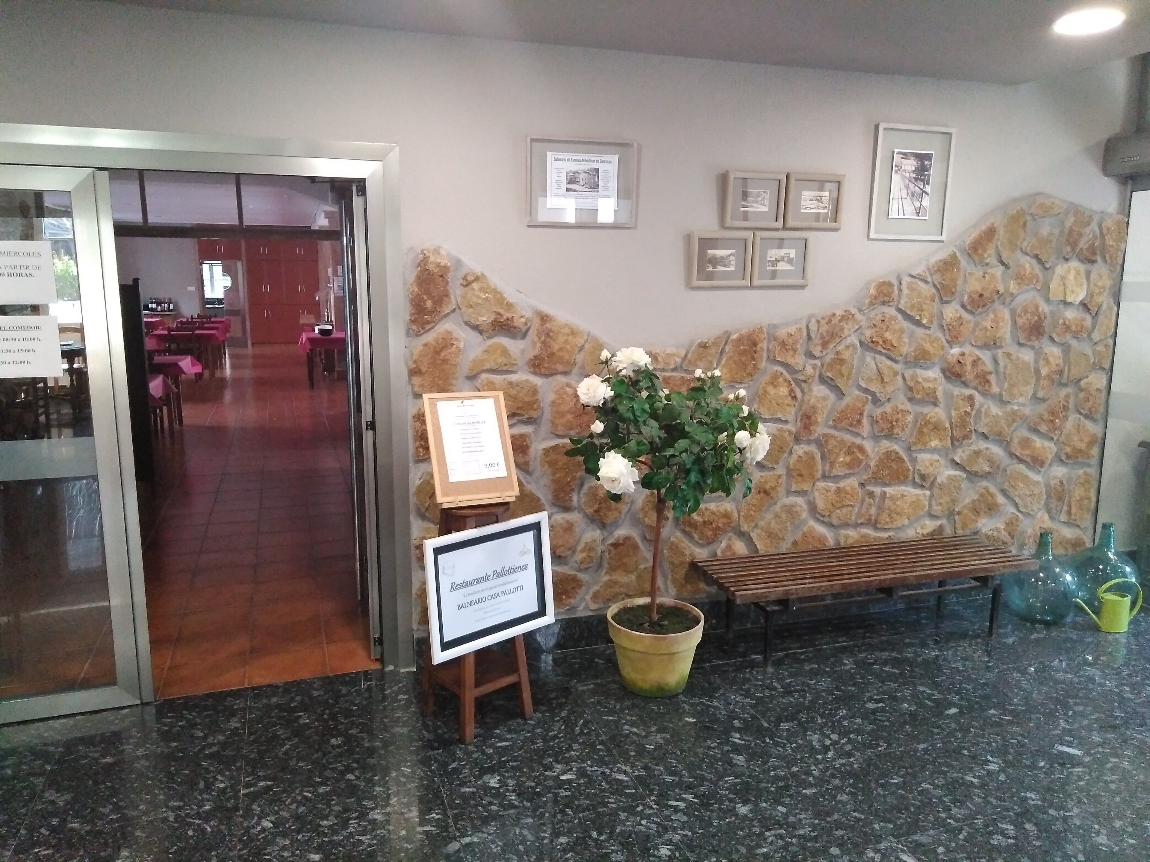 Um hall com parede de pedra, quadros nas paredes, uma planta em vaso e um banco de madeira.