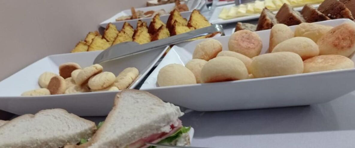 Buffet com diversos alimentos, incluindo sanduíches, pães e outros produtos de panificação.