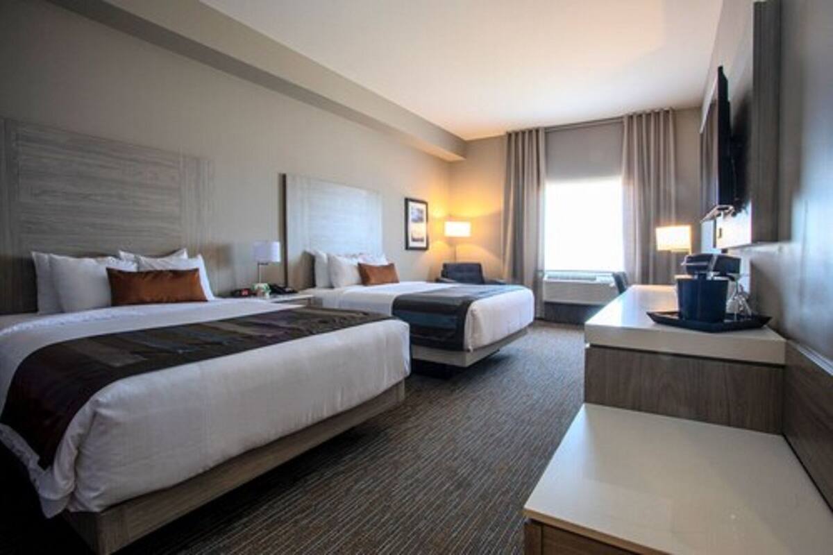 Quarto de hotel com duas camas, uma escrivaninha, televisão e janela com cortinas.