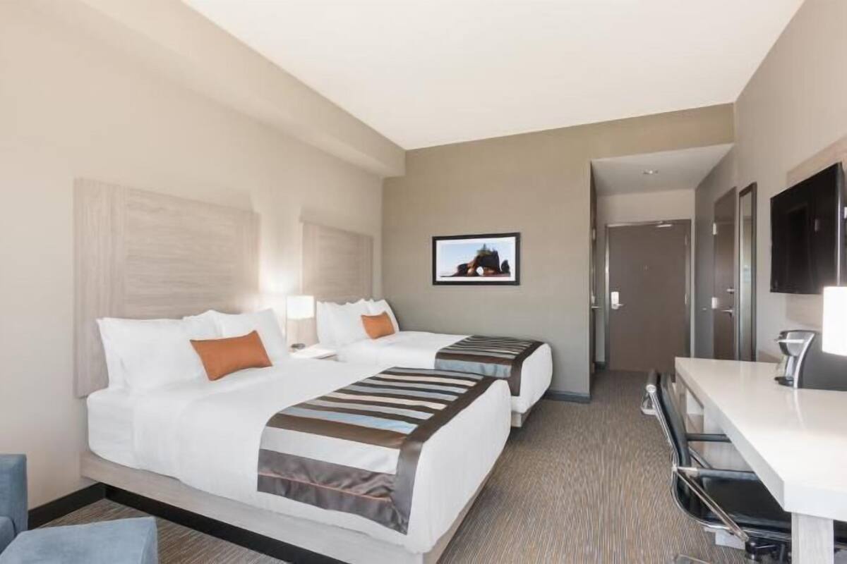 Quarto de hotel com duas camas, uma escrivaninha, uma cadeira e uma televisão.