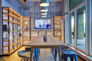 Uma sala de reuniões moderna com uma mesa comprida, cadeiras e prateleiras embutidas. Uma televisão está montada na parede e há grandes janelas que proporcionam luz natural.