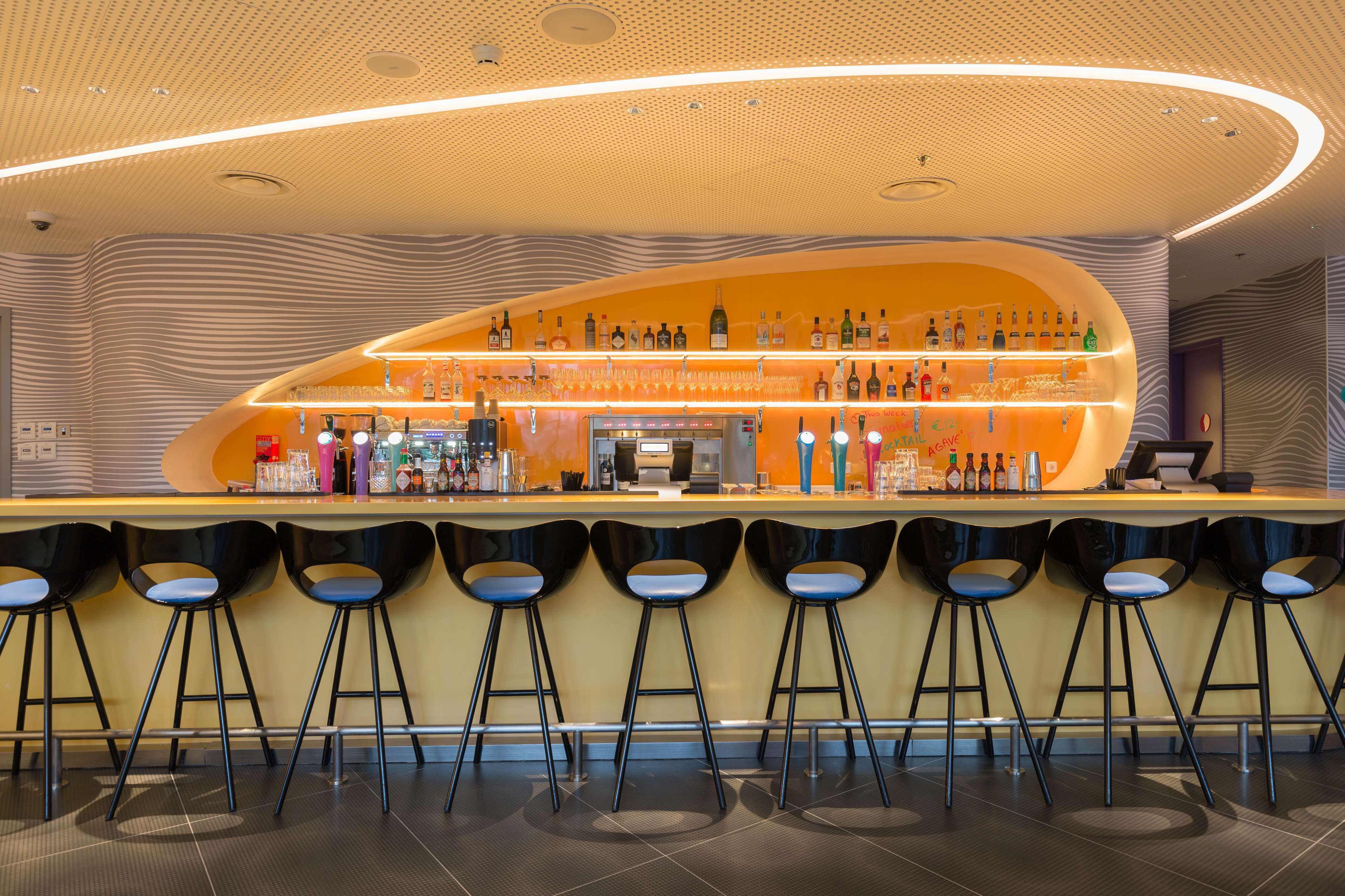 Um bar moderno com balcão curvo, vários bancos e uma variedade de garrafas e copos.