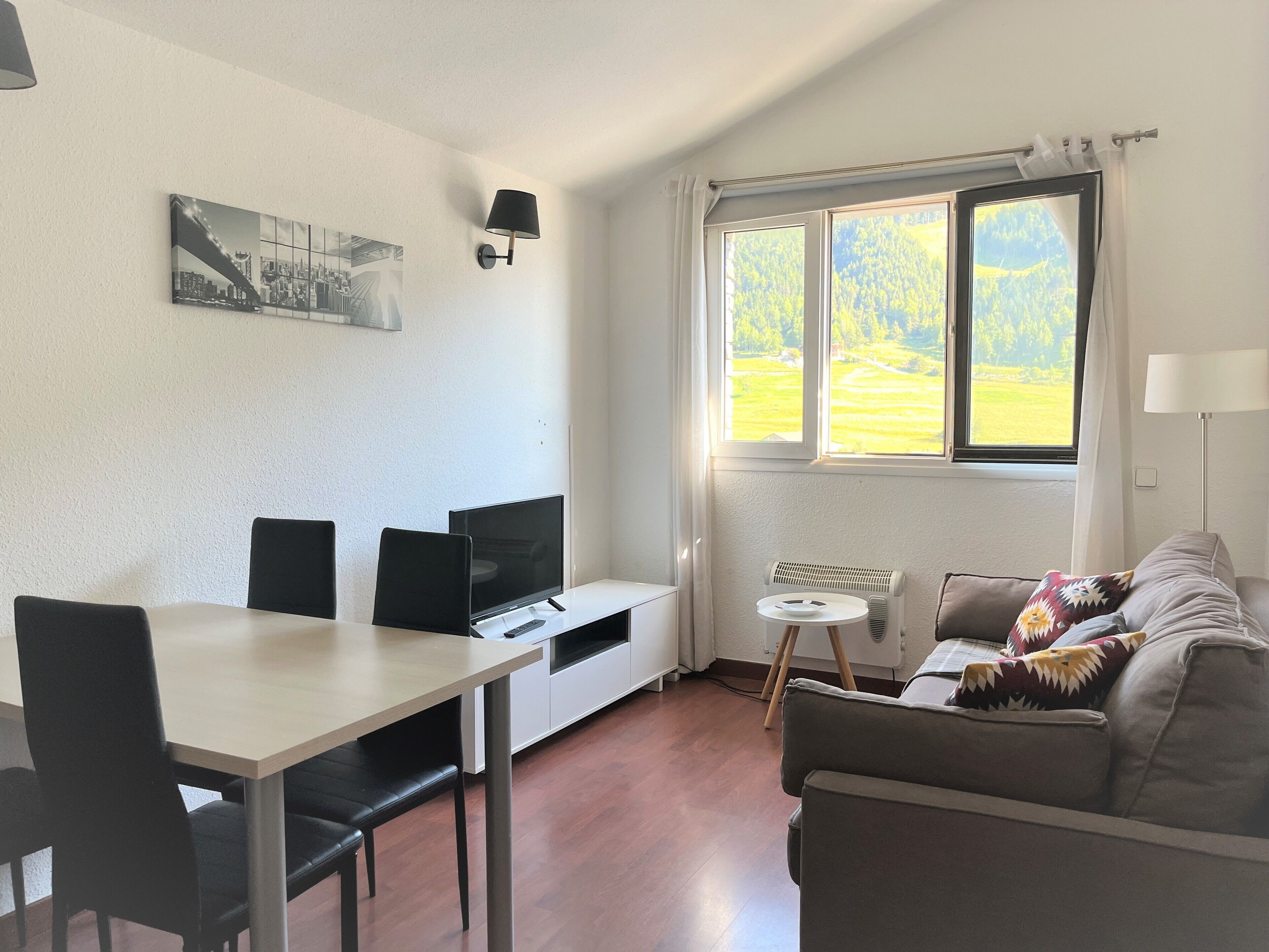 Quarto com uma mesa de jantar, cadeiras, sofá, radiador e janela com vista para uma paisagem verde.