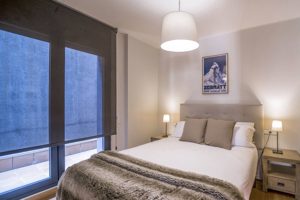 Quarto com uma cama grande, duas mesas de cabeceira com luminárias, uma janela com vista e um quadro na parede.