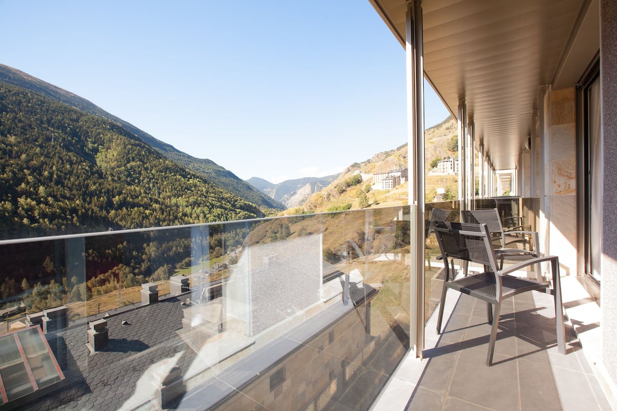 Varanda com guarda-corpo de vidro com vista para uma paisagem montanhosa.