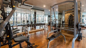 Uma academia com diversos equipamentos de ginástica, um espelho grande na parede e piso de madeira.