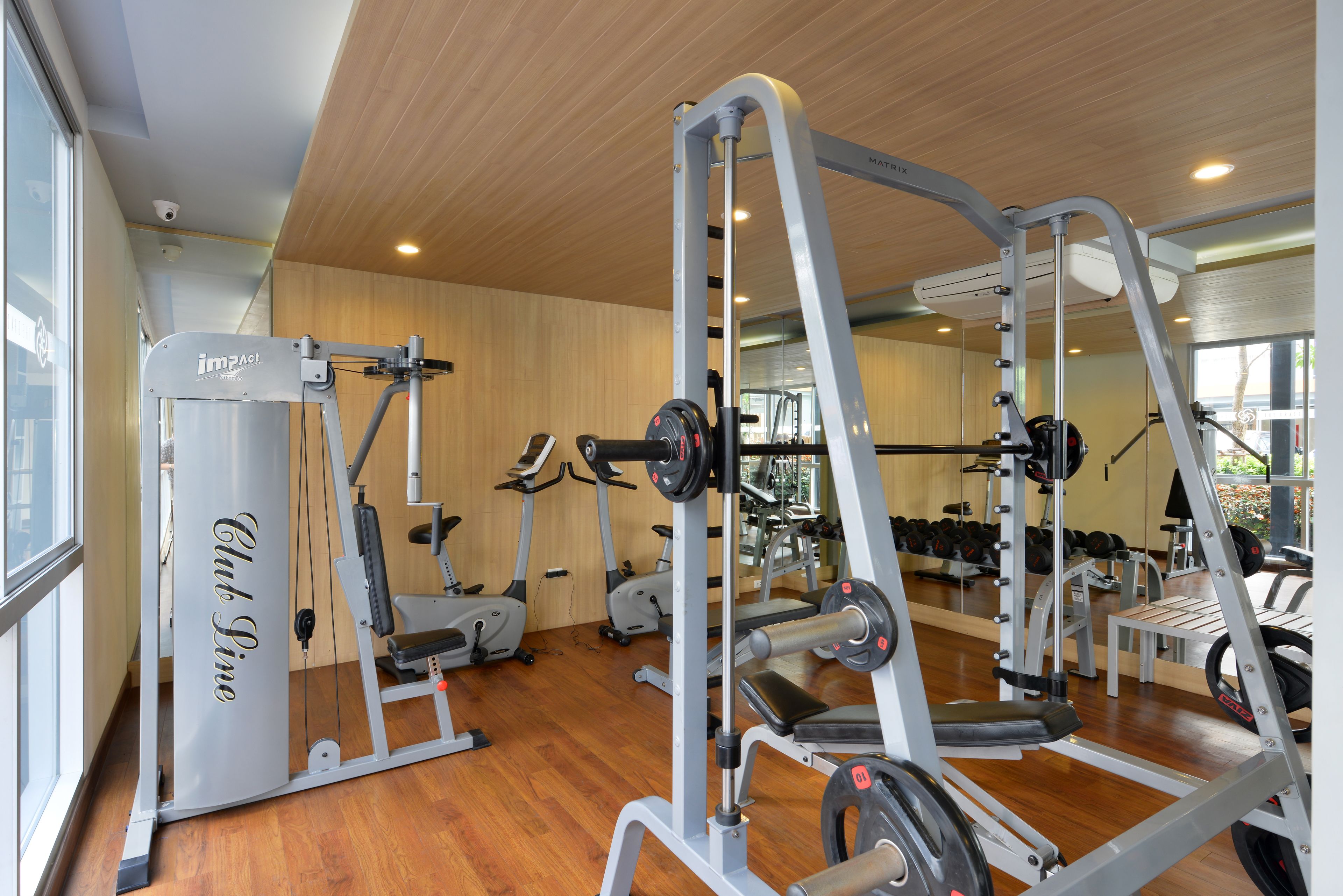 Uma academia com diversos equipamentos de exercício, um espelho e piso de madeira.
