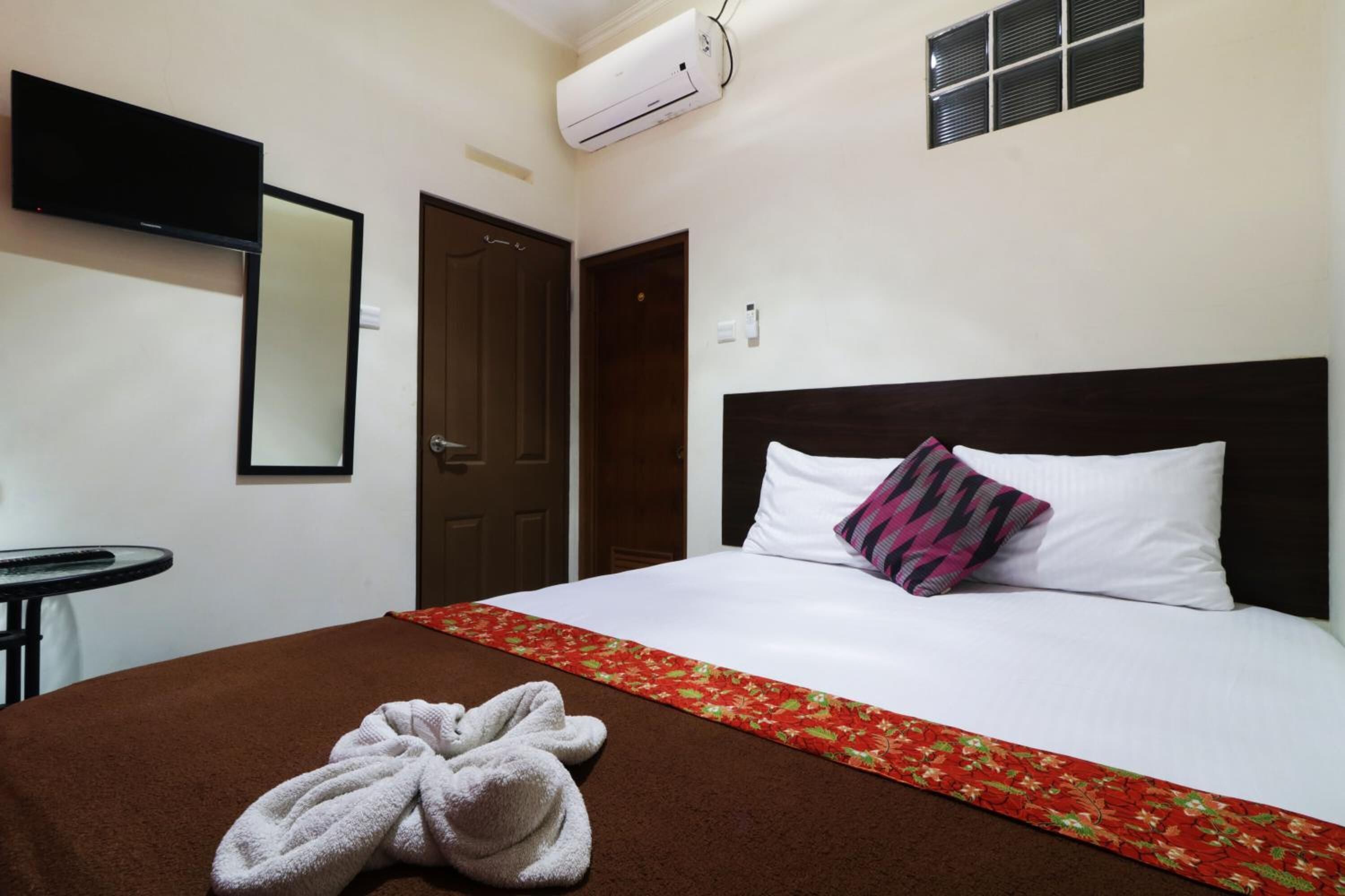Quarto de hotel com uma cama, televisão na parede, ar condicionado e uma porta.