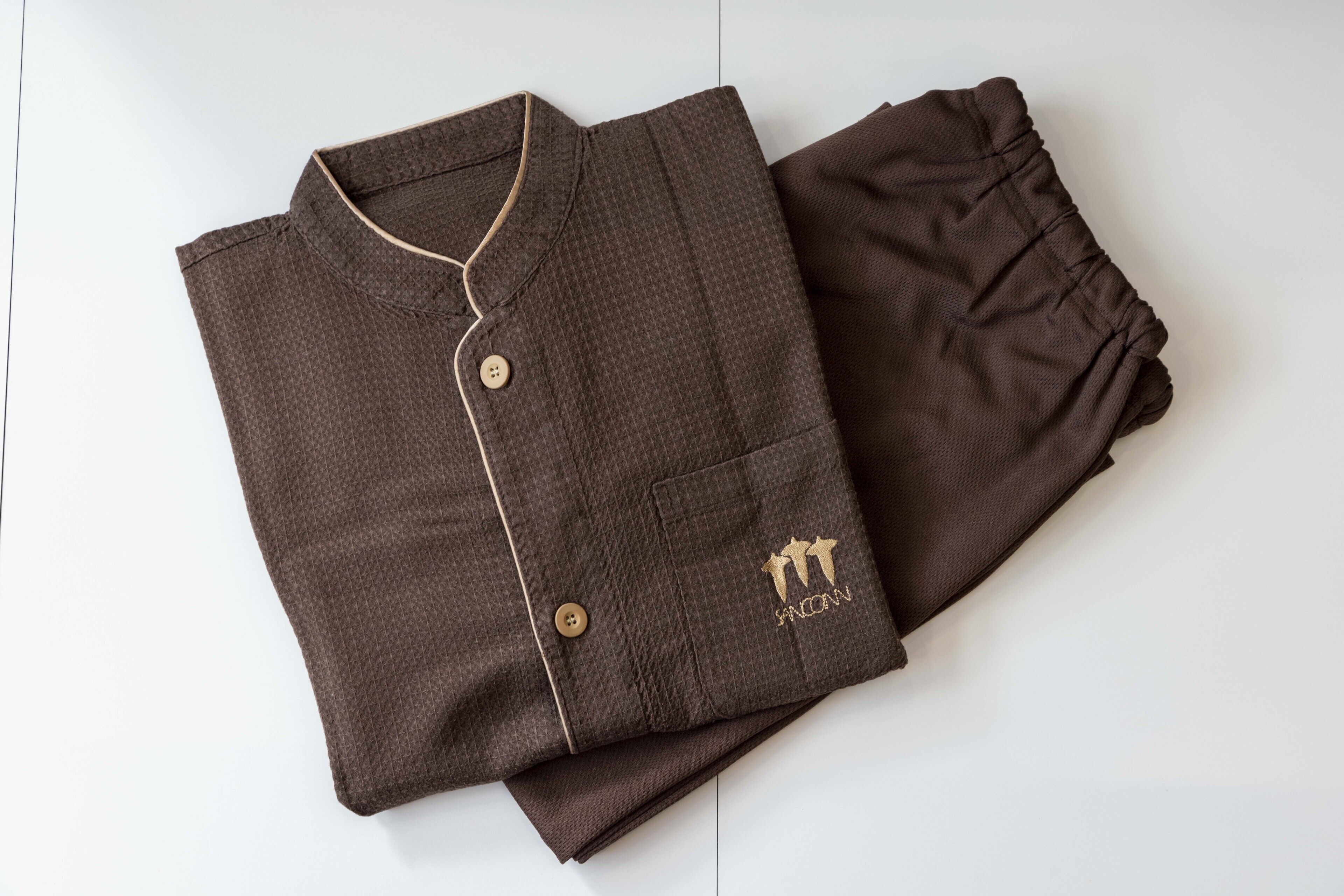 Uma camisa marrom bem dobrada, com colarinho e botões, e calças marrom combinando.