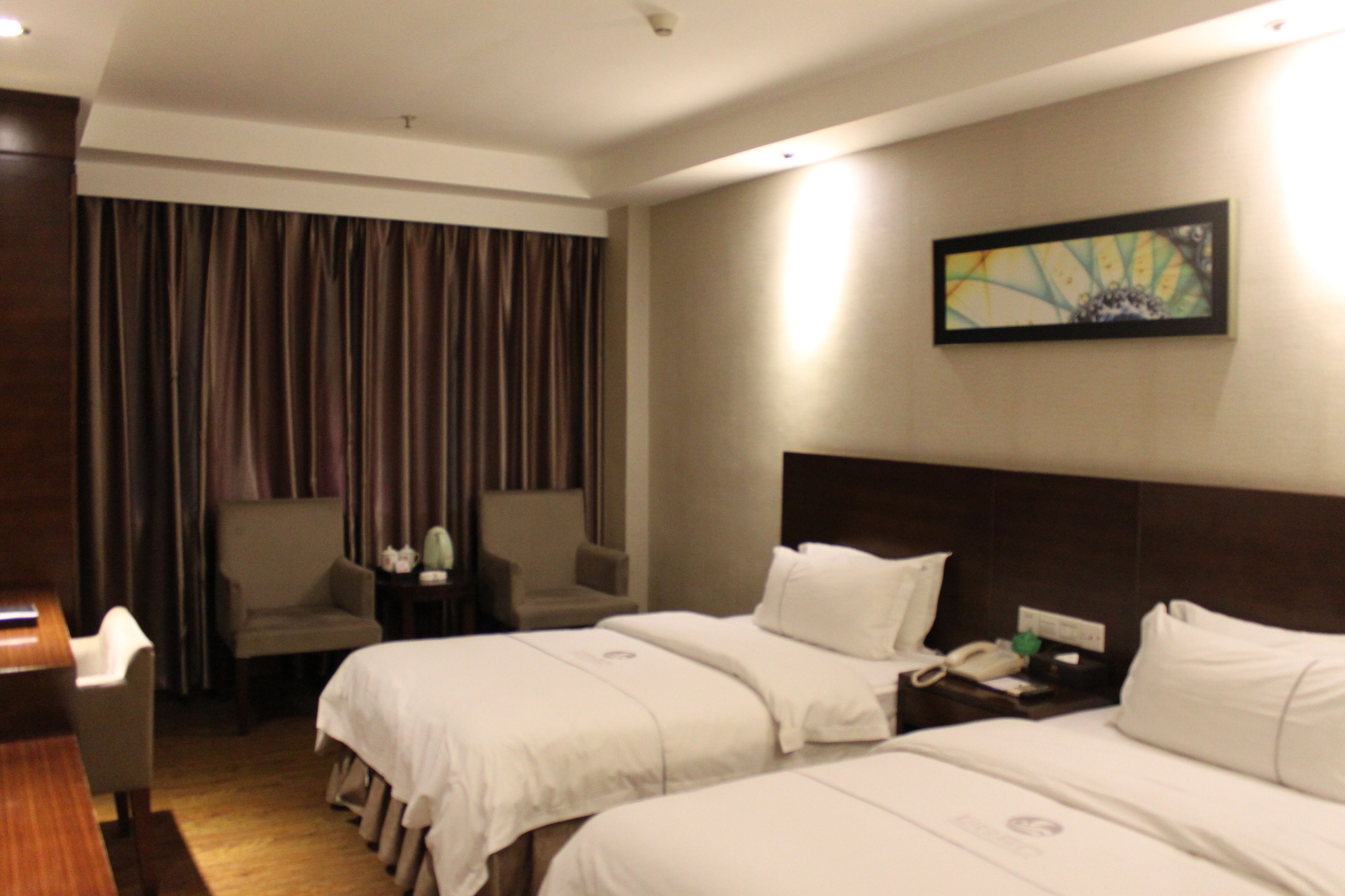 Quarto de hotel com duas camas, uma mesa, uma cadeira e um quadro na parede.