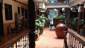 Um espaço interno amplo, com piso em azulejo, escada com guarda-corpo de metal e diversas plantas em vasos.