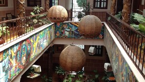 Um átrio em vários níveis com luminárias de vime suspensas, um mural colorido e plantas em vasos.