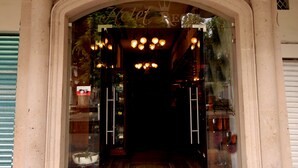 A entrada do Hotel Regis, com uma placa acima da porta, uma porta de vidro e um tapete de boas-vindas na entrada.