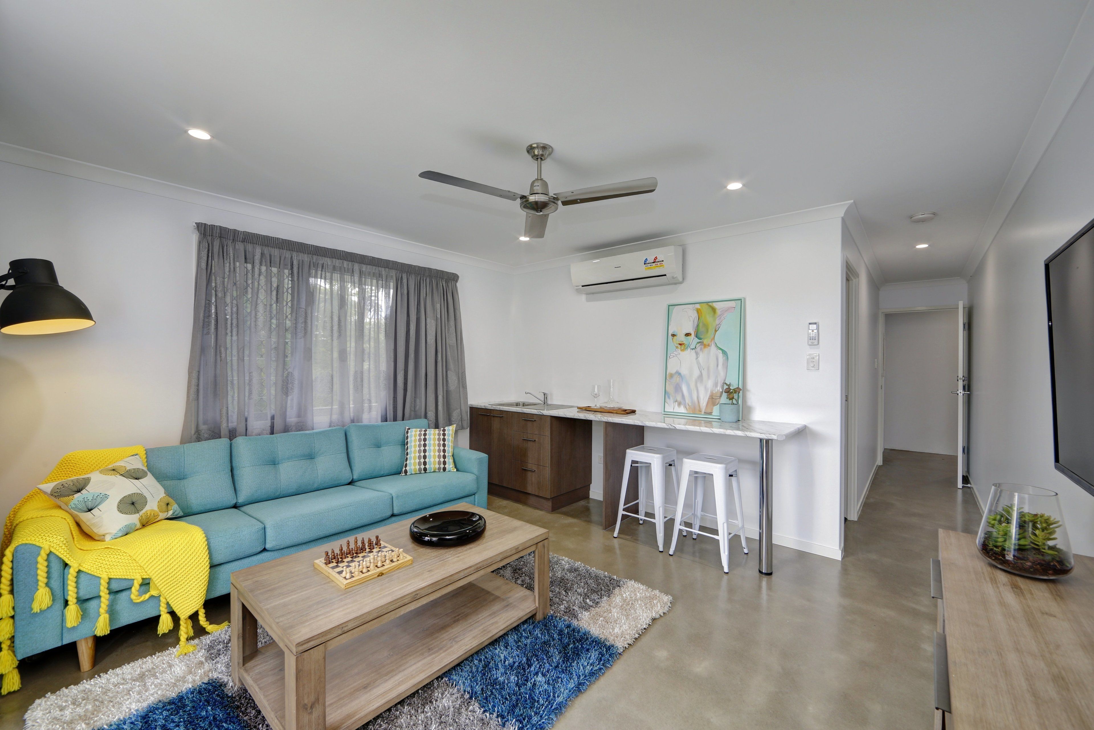 Uma sala de estar moderna com sofá, mesa de centro e um tabuleiro de xadrez. Há uma área de cozinha com um banco de bar e uma mesa de jantar.