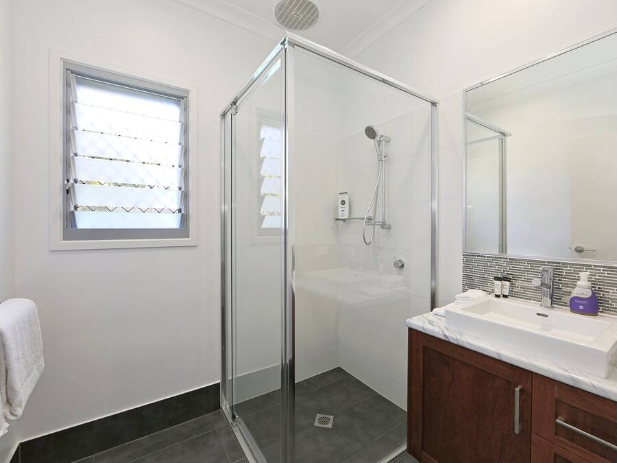 Casa de banho moderna com chuveiro em cabine de vidro, lavatório branco com bancada de mármore e um espelho grande acima do lavatório.