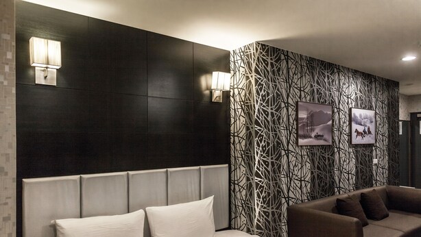 Quarto de hotel moderno com uma cama grande, um sofá marrom e uma parede estampada.