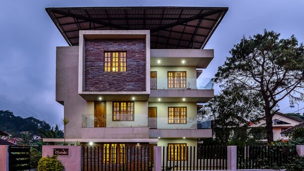 Uma casa moderna de vários andares com telhado plano, janelas amplas e portão fechado.