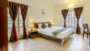Quarto de hotel bem arrumado, com cama, duas mesas de cabeceira com abajures, uma cadeira e um ventilador de teto.