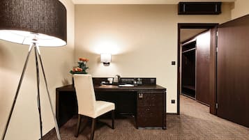 Quarto de hotel com escrivaninha, cadeira, abajur e uma pequena cozinha equipada.