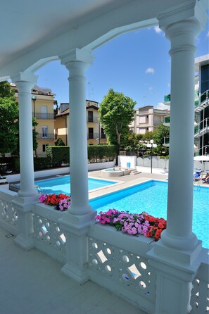 Área da piscina com colunas brancas e vista para edifícios ao redor.