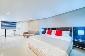 Quarto de hotel moderno com uma cama grande, área de estar e escrivaninha.