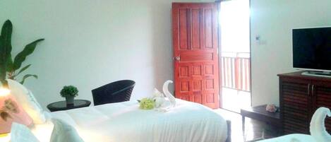 Quarto de hotel com duas camas, uma televisão, um armário de madeira, uma mesinha com uma planta e uma porta para o exterior.