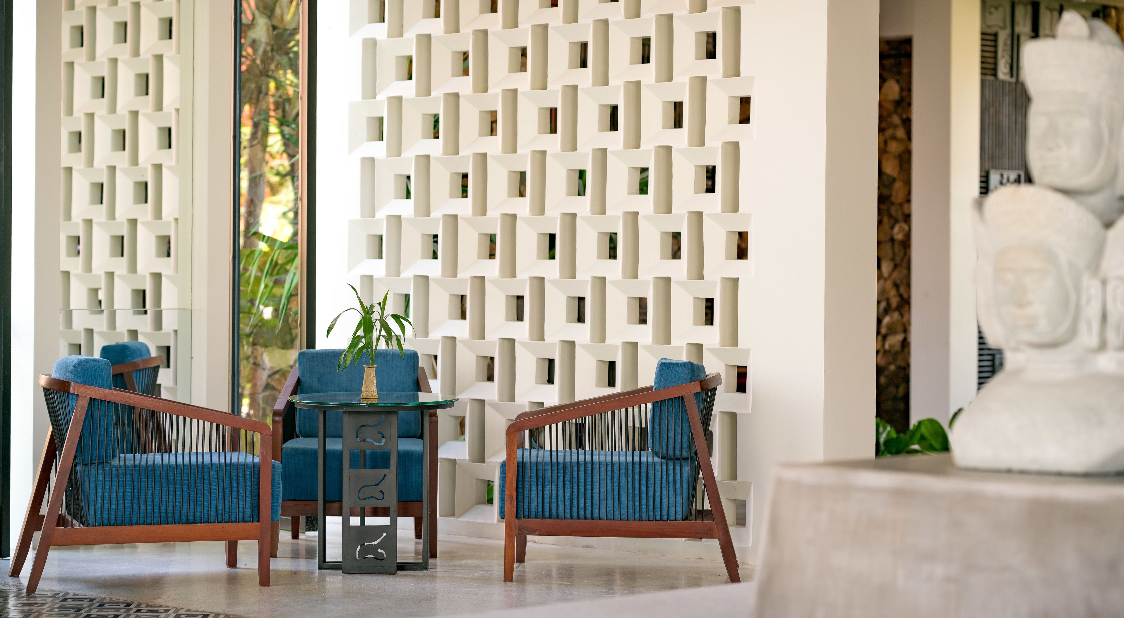 Um interior moderno com duas poltronas revestidas de azul, uma mesinha redonda e um painel de parede branco decorativo.