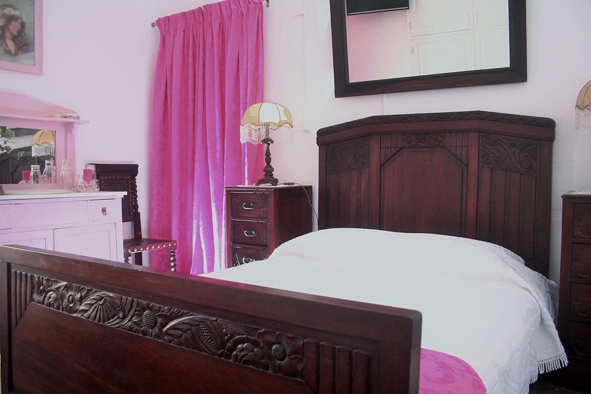 Quarto com cama de madeira, cômoda, espelho e cortina rosa.