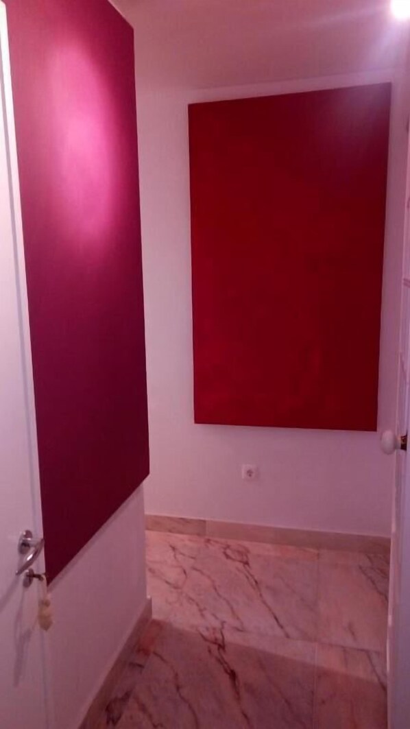 Quarto com parede de destaque vermelha, piso de mármore e uma porta.