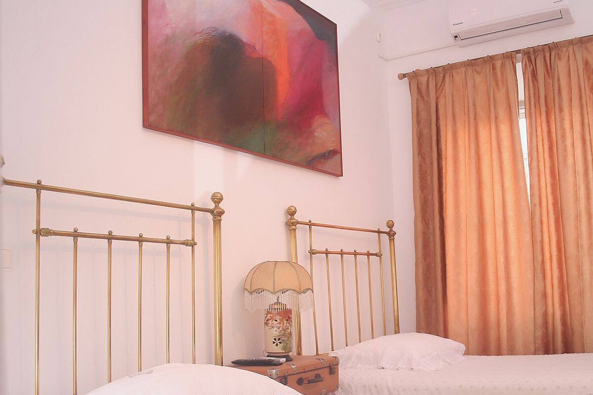 Quarto com duas camas, um quadro na parede e uma janela com cortinas.