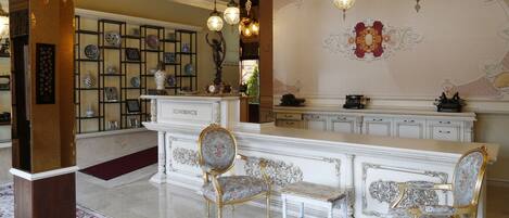 Um lobby luxuoso com lustres elaborados, um balcão de recepção de mármore e cadeiras clássicas.